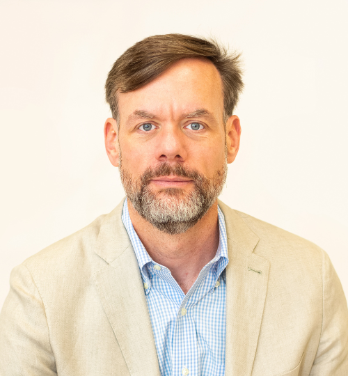 A middle aged man with brown hair and a greying goatee, wearing a blue ...